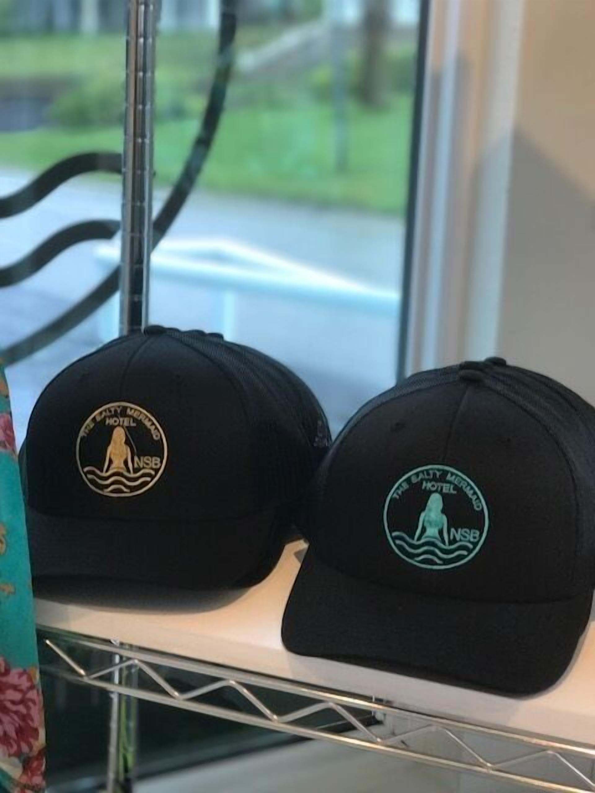 Dois bonés pretos com logotipos em uma prateleira de metal.