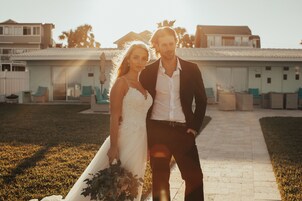 Um casal a rigor de casamento posado num pátio com um edifício ao fundo.