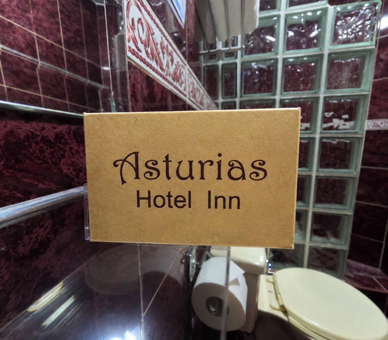 Placa do Asturias Hotel Inn num banheiro com parede de mármore e box de vidro.