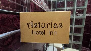 Placa do Asturias Hotel Inn num banheiro com parede de mármore e box de vidro.