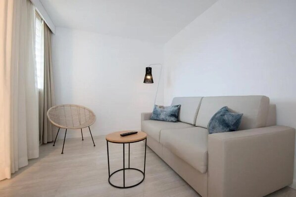 Uma sala de estar moderna com um sofá bege, uma poltrona redonda de vime, uma mesinha de madeira e um abajur.