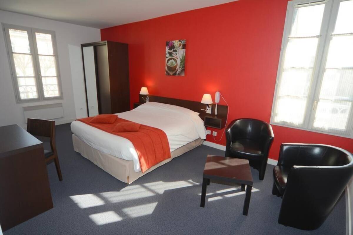 Quarto de hotel com cama, escrivaninha, cadeira, guarda-roupa e janela.