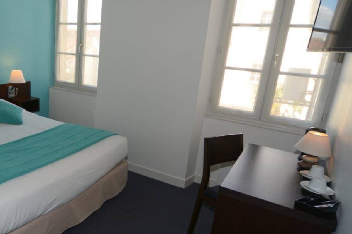 Quarto com cama, duas mesas de cabeceira com luminárias, escrivaninha com cadeira e janela.