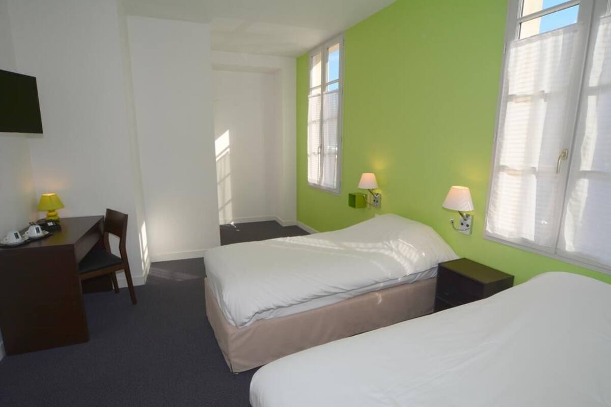 Quarto de hotel com duas camas, uma escrivaninha e duas luminárias.