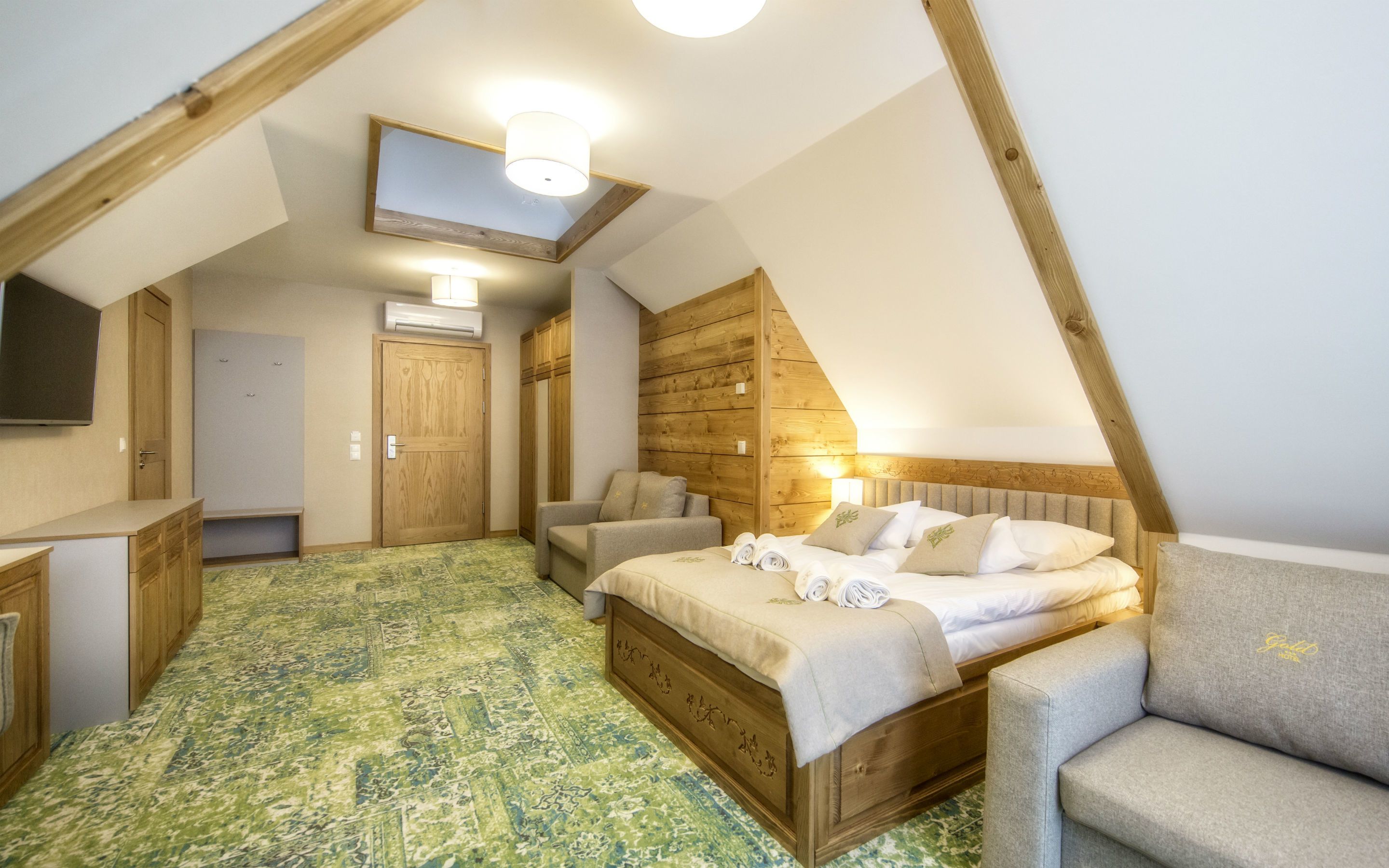 Quarto com teto inclinado, uma cama com cabeceira, uma cadeira, guarda-roupa e espelho.