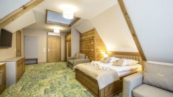Quarto com teto inclinado, uma cama com cabeceira, uma cadeira, guarda-roupa e espelho.