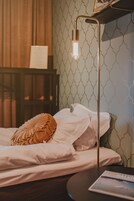 Cama bem arrumada com lençóis brancos, um travesseiro decorativo marrom e uma mesa de cabeceira com uma revista.