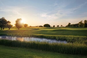Um campo de golfe com lago, árvores e céu limpo.