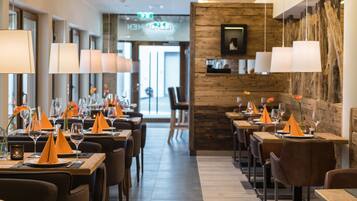 Restaurante com mesas preparadas para refeições, apresentando um interior moderno com detalhes em madeira e iluminação pendente.