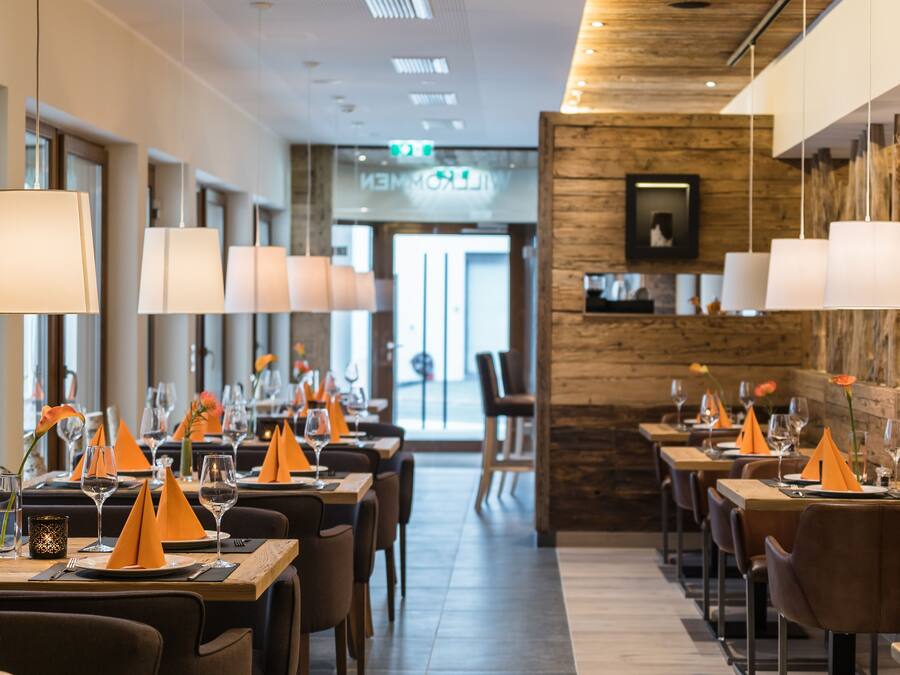 Restaurante com mesas preparadas para refeições, apresentando um interior moderno com detalhes em madeira e iluminação pendente.