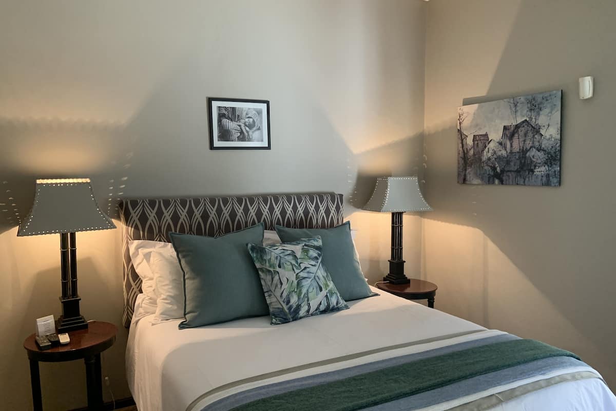 Cama bem arrumada com manta listrada, duas luminárias laterais e um quadro pendurado acima.