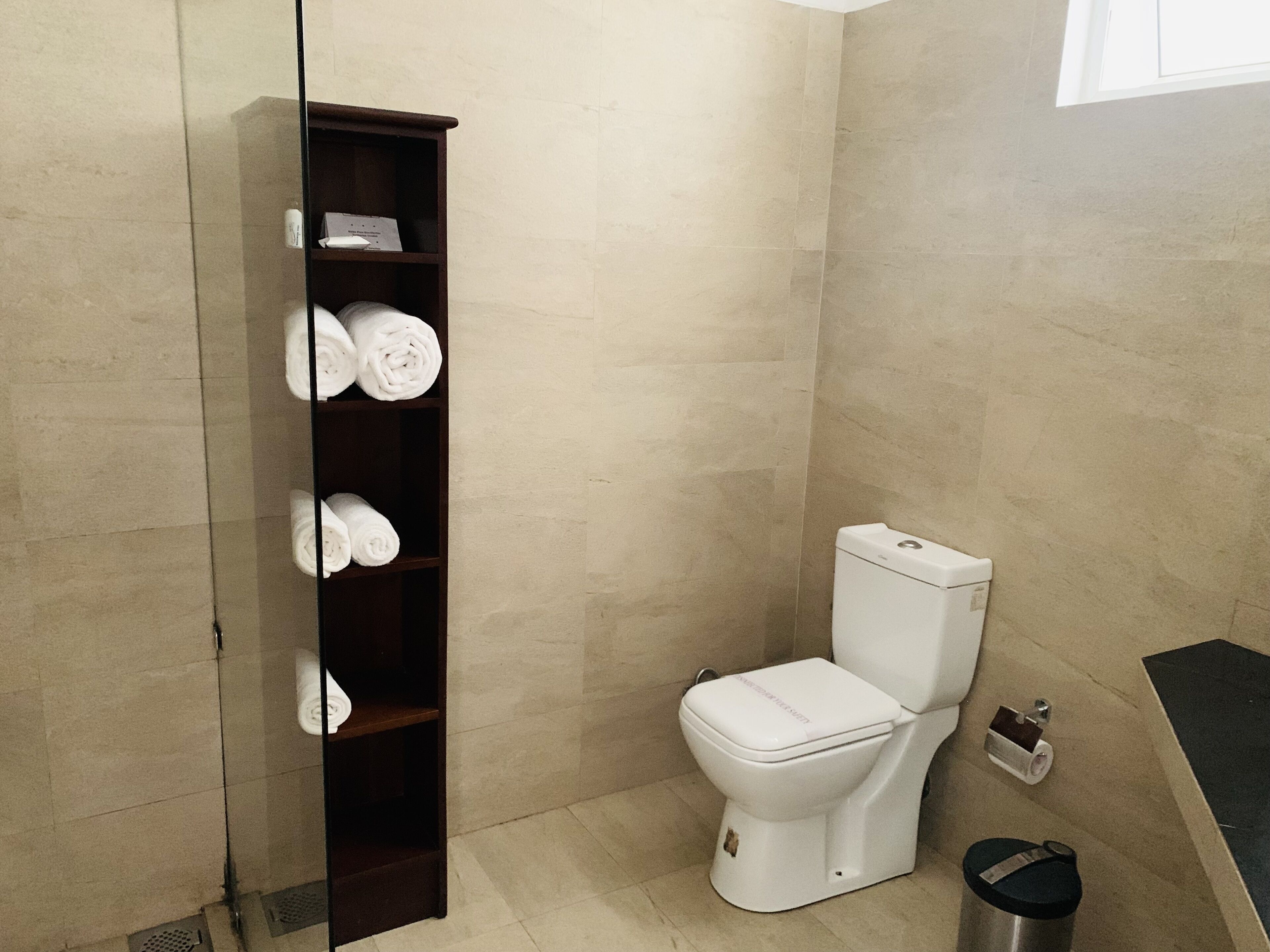 Um banheiro com vaso sanitário, porta-toalhas com toalhas e um cesto de lixo.