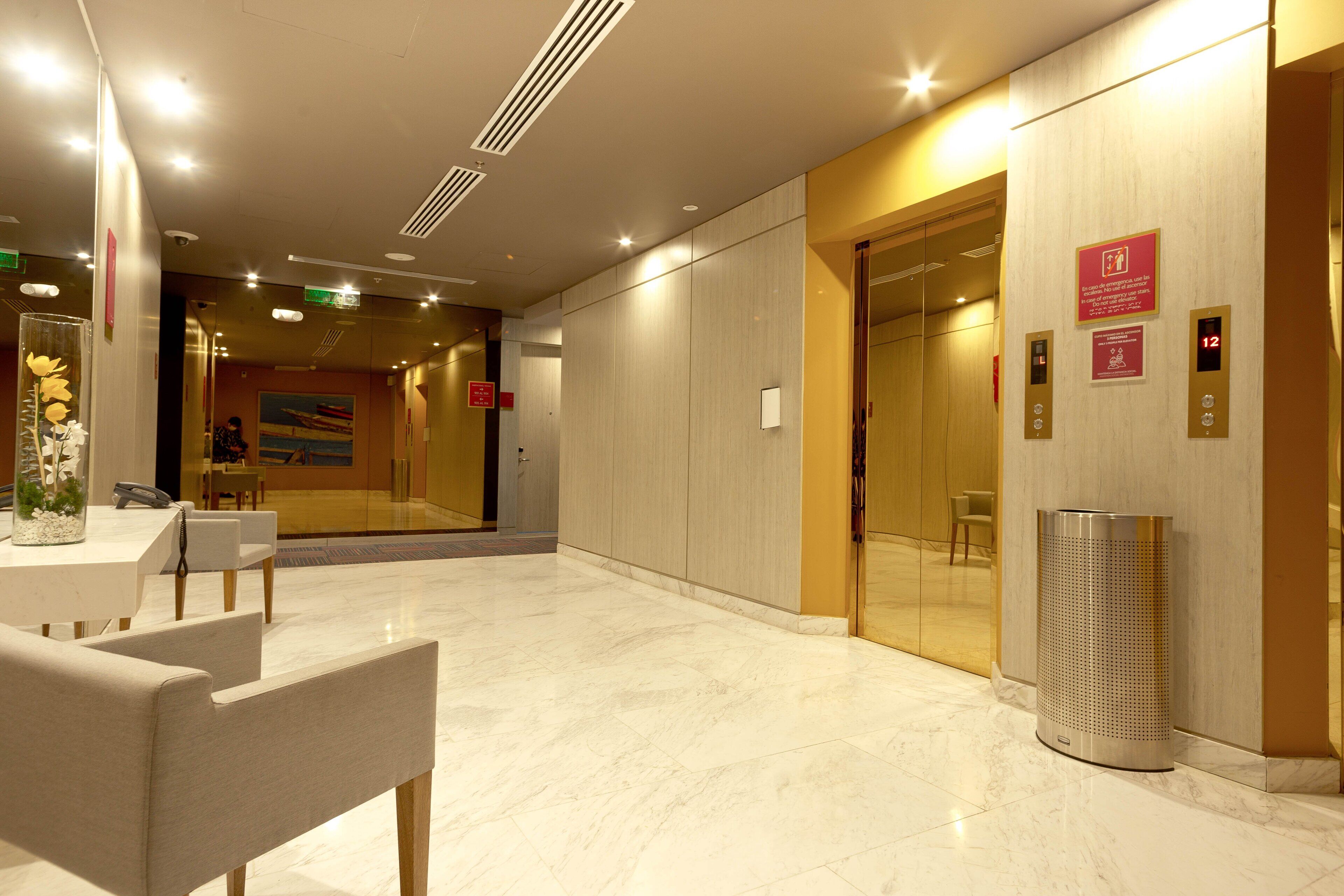 Um saguão de hotel com balcão de recepção, área de estar e elevador.