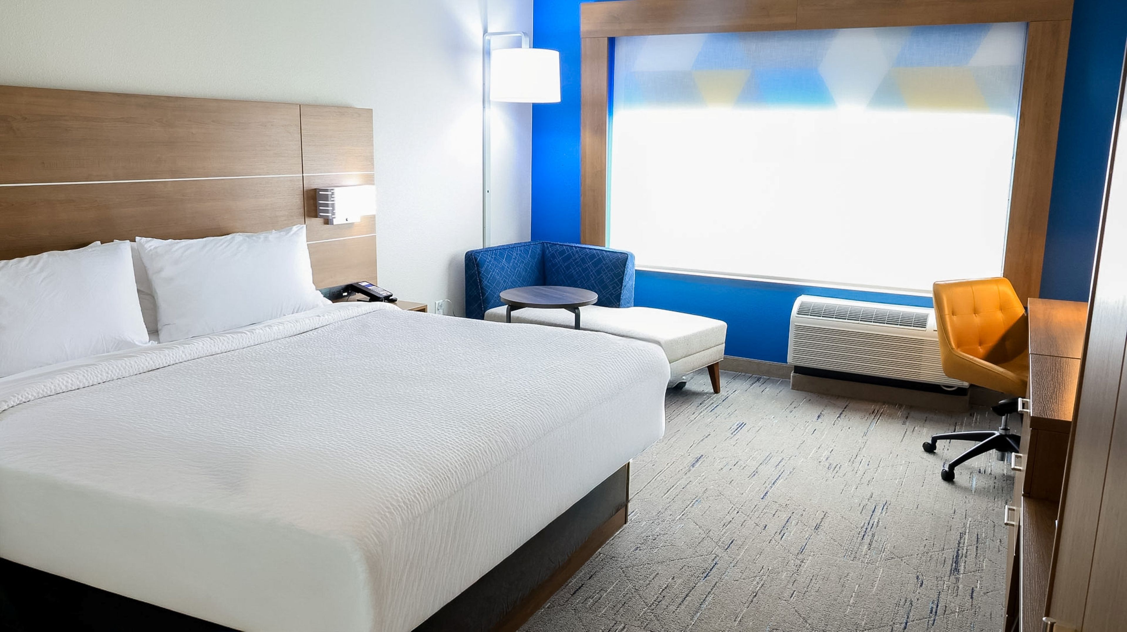Quarto de hotel com uma cama grande, escrivaninha, cadeira e janela com vista.