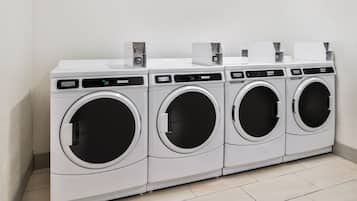 Quatro máquinas de lavar roupa brancas, do tipo frontal, dispostas em linha em um ambiente comercial.