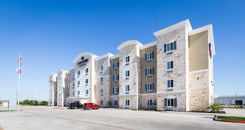 Um hotel com vários andares, fachada de pedra, diversas janelas e um estacionamento com carros.
