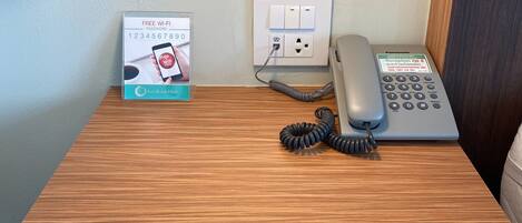 Mesa de madeira com telefone, cabo de extensão enrolado e sinal indicando senha de Wi-Fi gratuita.