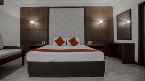 Quarto de hotel com uma cama grande, duas mesas de cabeceira, um criado-mudo, um espelho e uma cabeceira com design acolchoado.