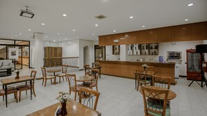 Uma ampla área de refeições com várias mesas e cadeiras de madeira, uma cozinha com armários de madeira e um espaço de estar com sofá e mesa de centro.