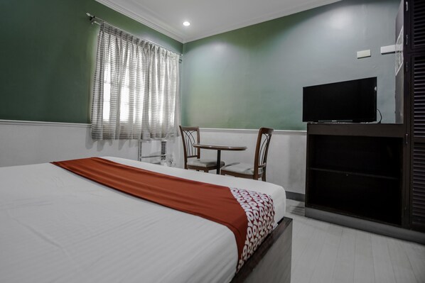 Quarto de hotel com cama, televisão, escrivaninha e cadeira.