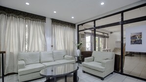 Uma sala de estar moderna com dois sofás, uma mesa de centro de vidro e uma janela grande com cortinas.
