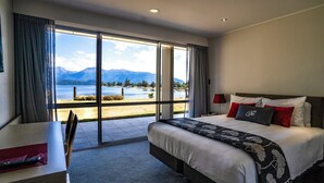 Quarto de hotel com uma cama grande, uma mesa e vista para montanhas e um lago.