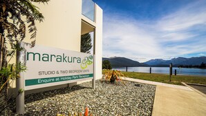 Um edifício com uma placa indicando 'marakura', com estúdios e apartamentos de dois quartos, e vista para montanhas e um lago.