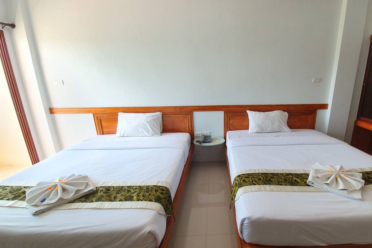 Quarto de hotel com duas camas individuais, uma mesa de cabeceira com telefone e uma cabeceira de madeira.