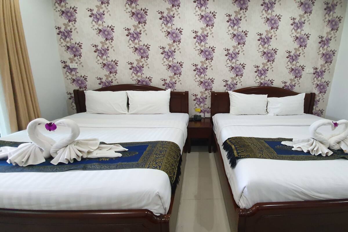 Quarto de hotel com duas camas, papel de parede floral e toalhas dobradas em forma de cisnes.