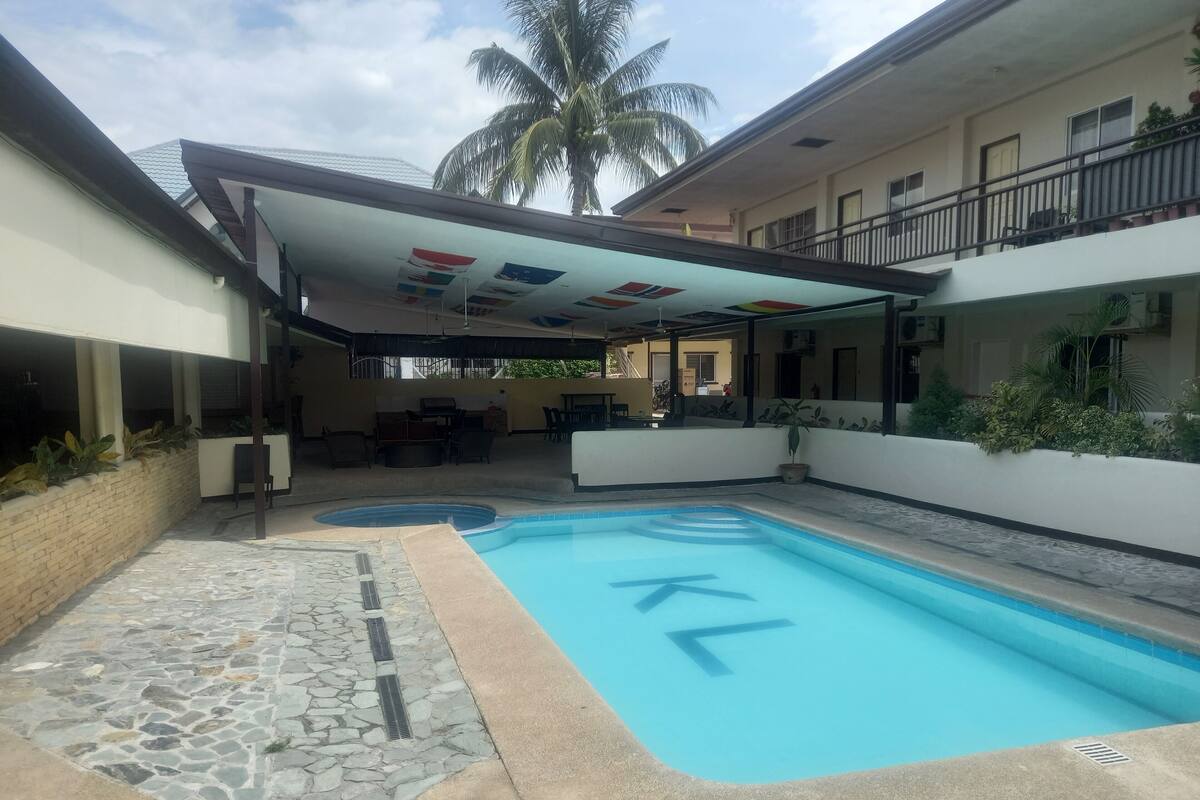 Piscina com deck revestido, área de estar coberta e uma palmeira ao fundo.