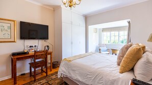Quarto com cama, escrivaninha com computador, televisão e janela com cortinas.