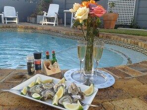 Mesa à beira da piscina com ostras, fatias de limão e duas garrafas de molho Tabasco.