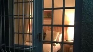 Quarto com cama, mesa de cabeceira e janela com vista para o exterior.