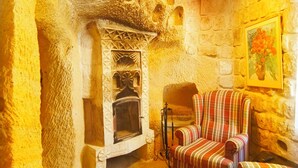 Um quarto de paredes de pedra com lareira, poltronas listradas e um tapete vermelho.