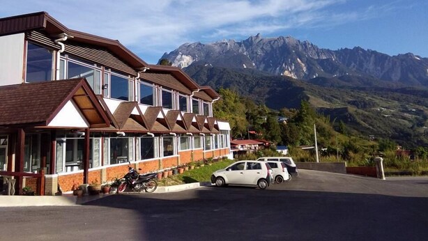 Um hotel com arquitetura moderna, apresentando uma fileira de quartos com grandes janelas, área de estacionamento e um cenário montanhoso.