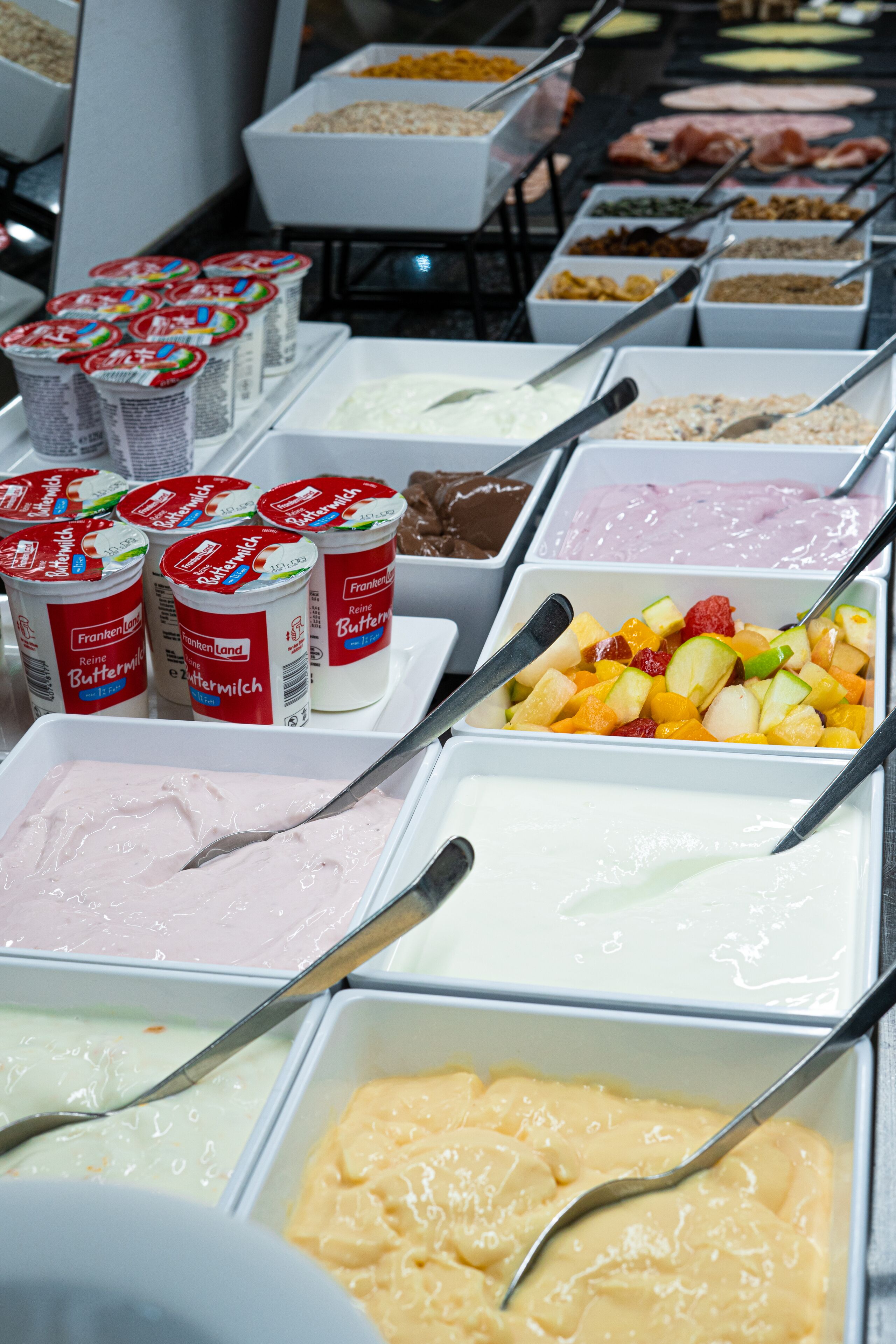 Buffet com diversos alimentos, incluindo iogurte, frutas e diferentes tipos de patês.