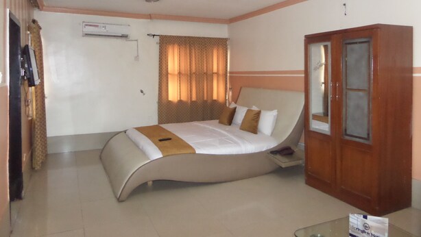 Quarto de hotel com cama curva, guarda-roupa de madeira e janela com cortinas.