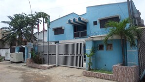 Um edifício de dois andares com fachada azul, portão de entrada e área de piscina.