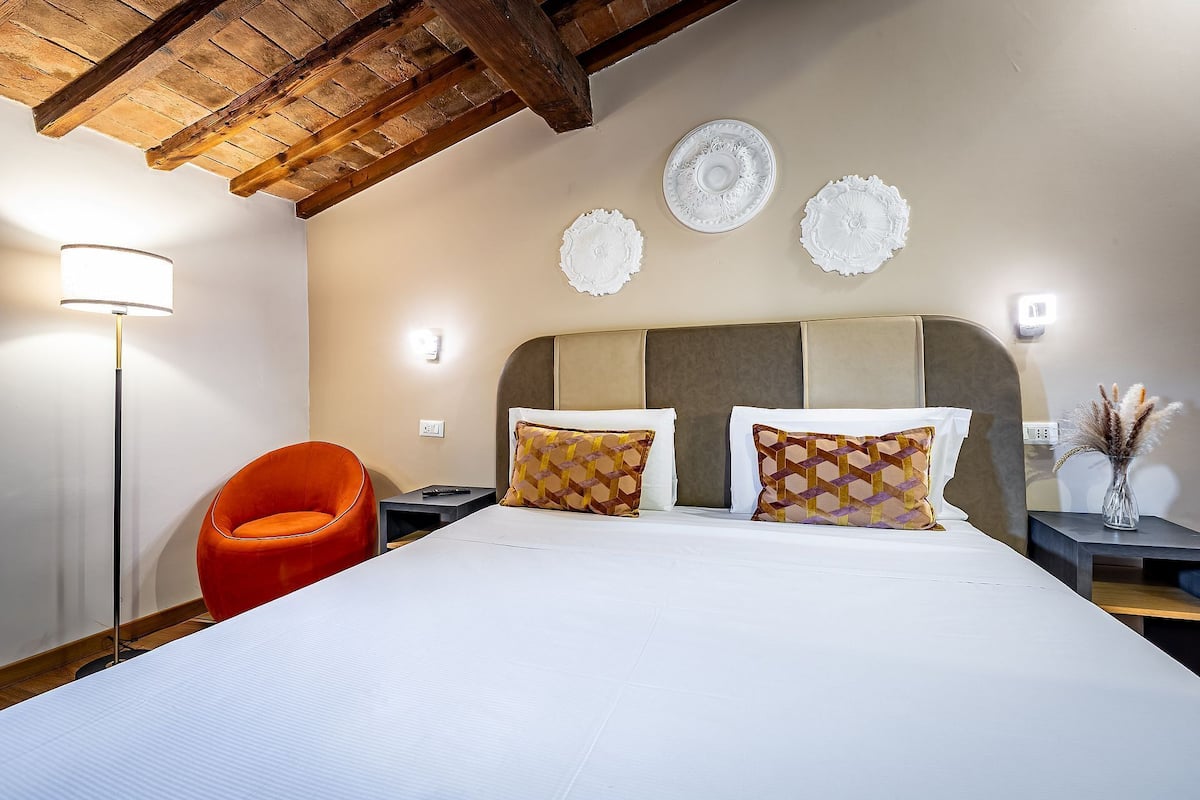 Quarto de hotel com uma cama, mesa de cabeceira, abajur e uma cadeira.