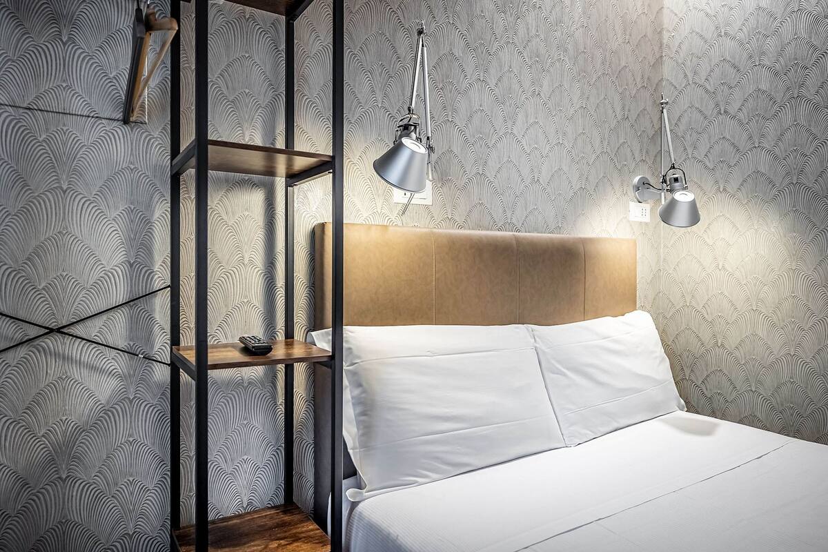 Uma cama bem arrumada com lençóis brancos, cabeceira de madeira e duas luminárias de cabeceira.