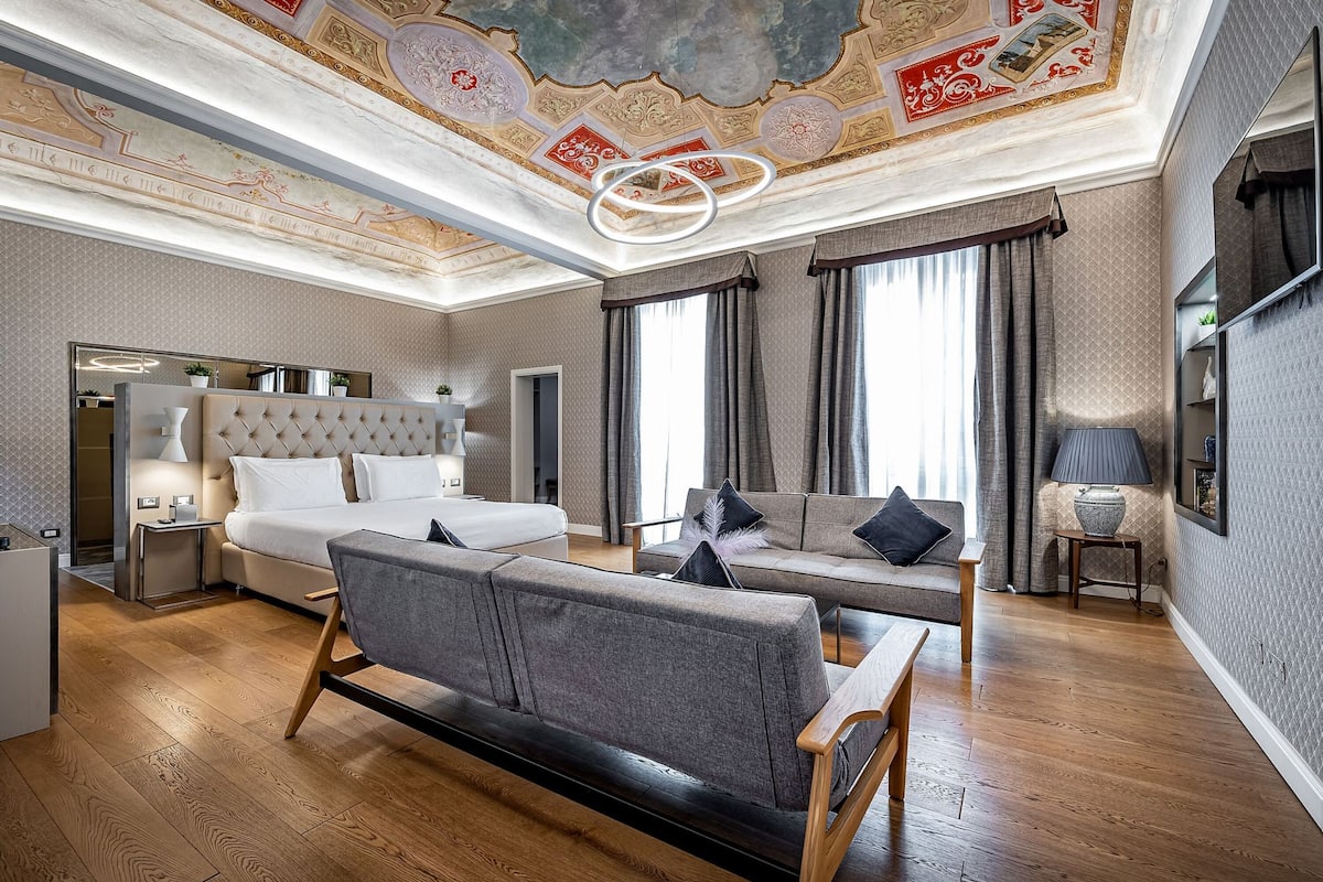 Quarto de hotel com uma cama grande, um sofá, uma escrivaninha e um espelho.