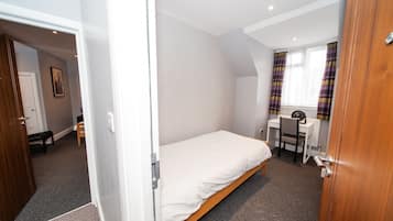 Quarto com uma cama de solteiro, escrivaninha e cadeira. Há uma porta que dá para outro cômodo e uma janela com cortinas.