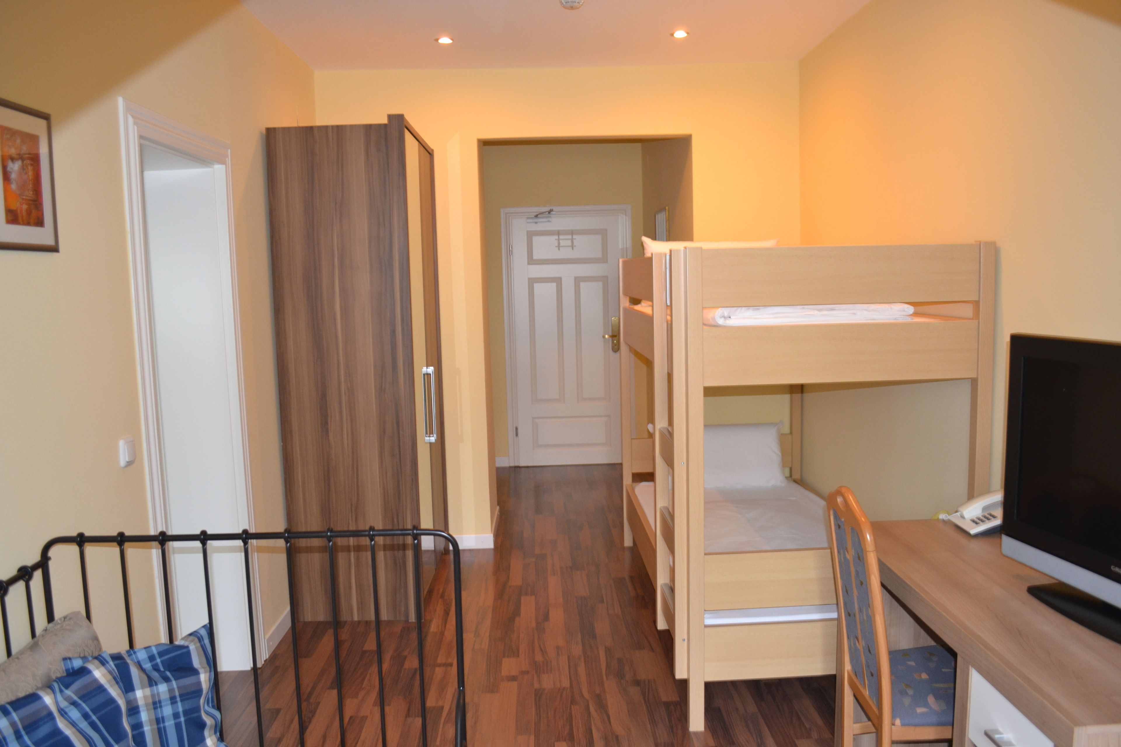 Quarto com beliche, escrivaninha e cadeira, televisão e porta para outro cômodo.