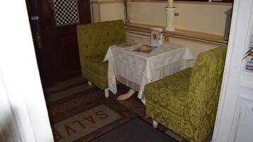 Um quarto com duas poltronas verdes estofadas, uma mesa pequena com toalha branca e um tapete estampado com a palavra "SALUTE".