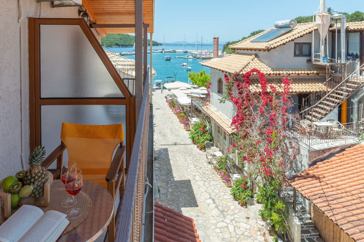 Uma varanda com vista para uma marina, um caminho de pedras e um edifício com flores vermelhas.