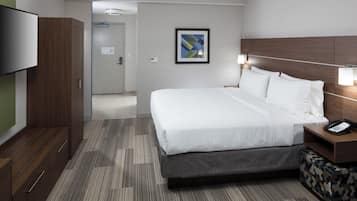 Quarto de hotel com cama, mesa de cabeceira, abajur e televisão à esquerda.