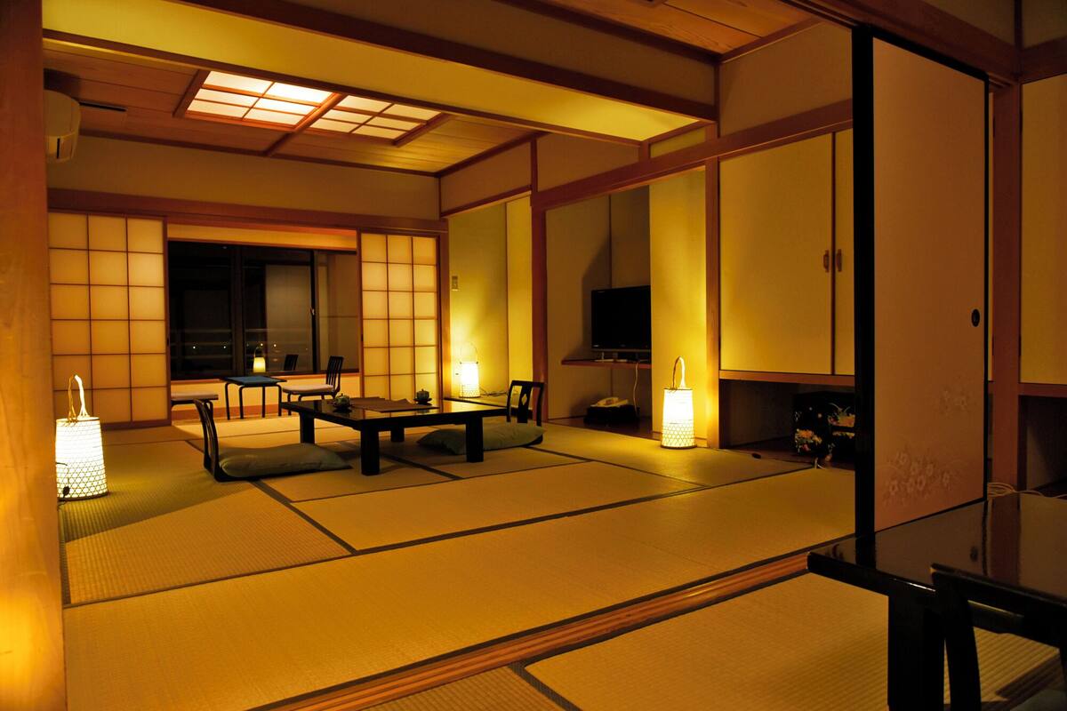 Um quarto japonês tradicional com tatames, uma mesa baixa com almofadas e portas deslizantes.