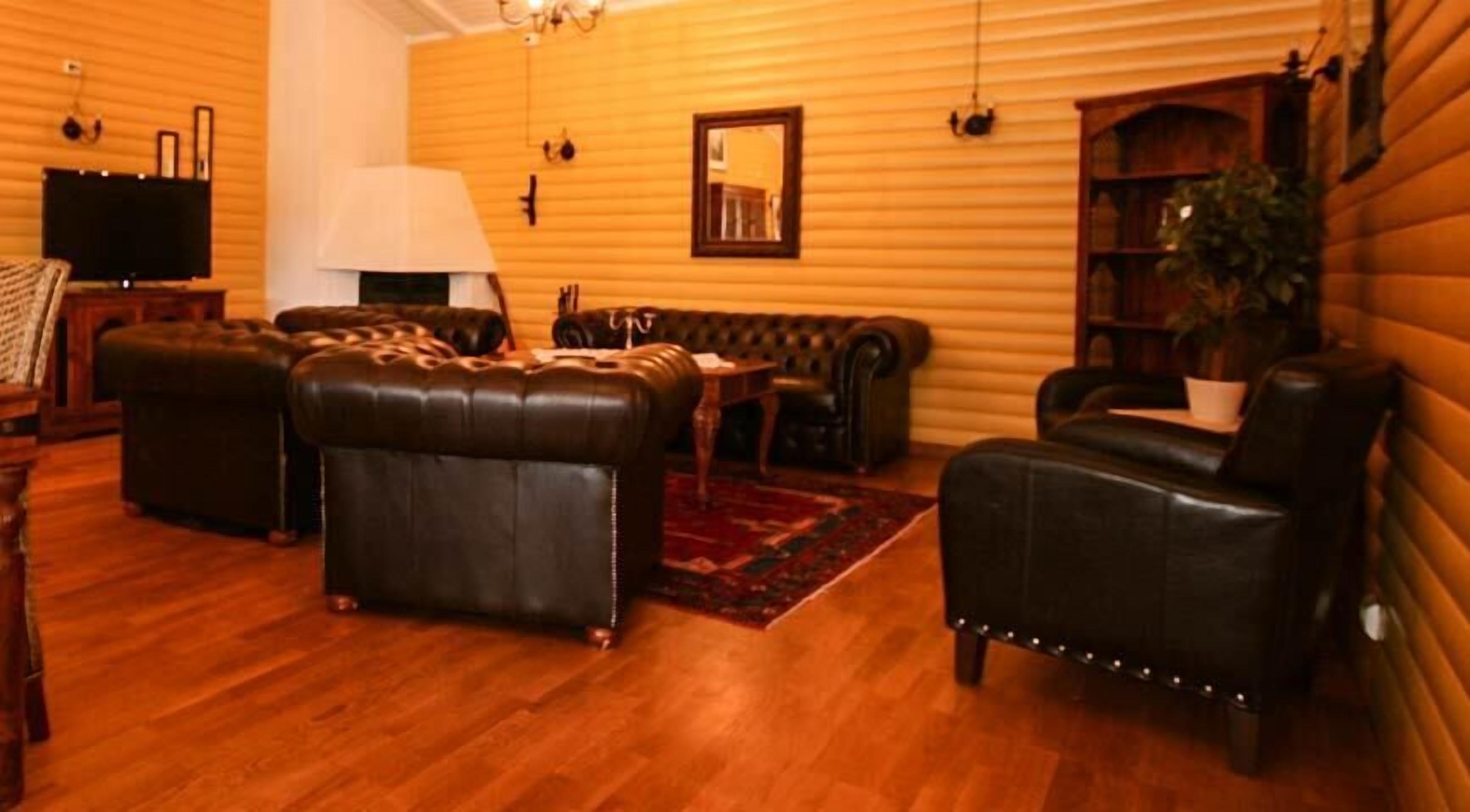 Uma sala de estar acolhedora, com um sofá de couro, um banquinho e uma poltrona, piso de madeira e uma televisão.