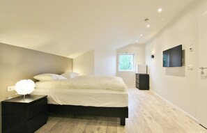 Quarto moderno com cama, mesa de cabeceira e televisão fixada na parede.