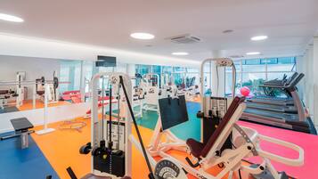 Uma academia com diversos equipamentos de exercícios, esteira e espelho.
